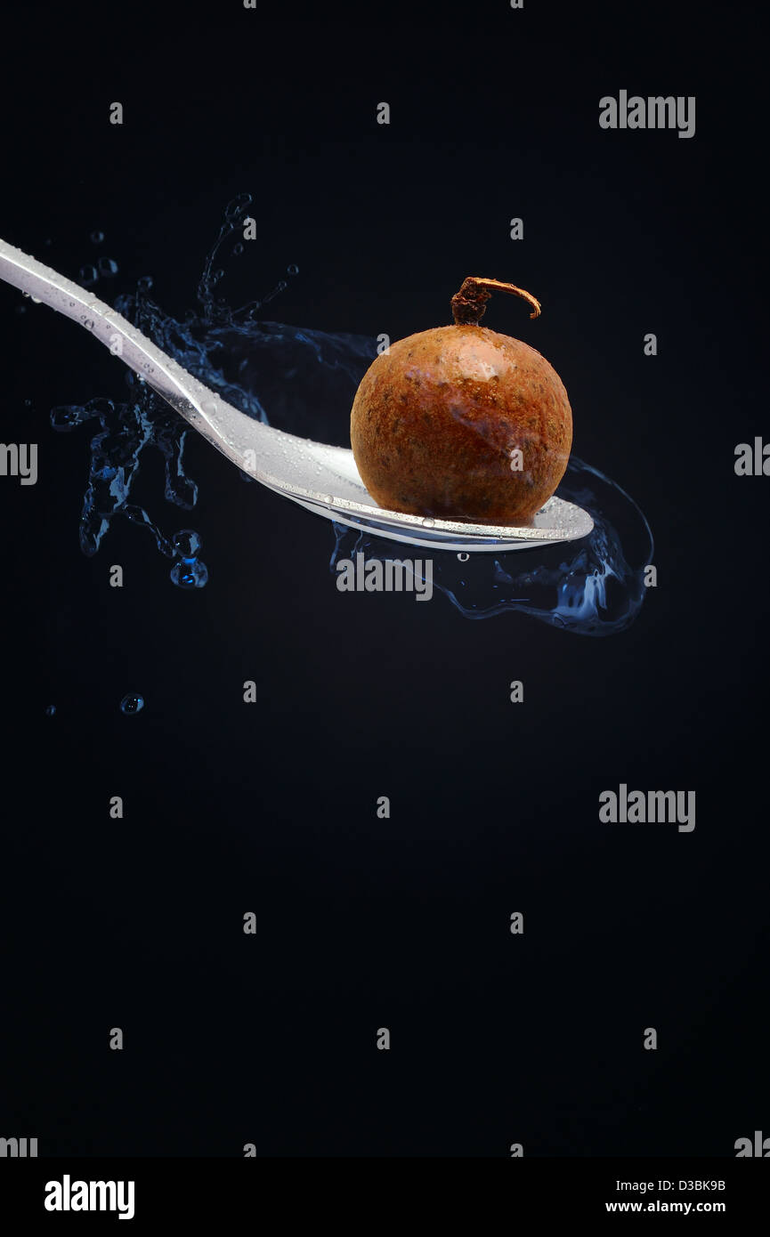 Teaspoon with longan fruit and dripping natural mineral water in black ...