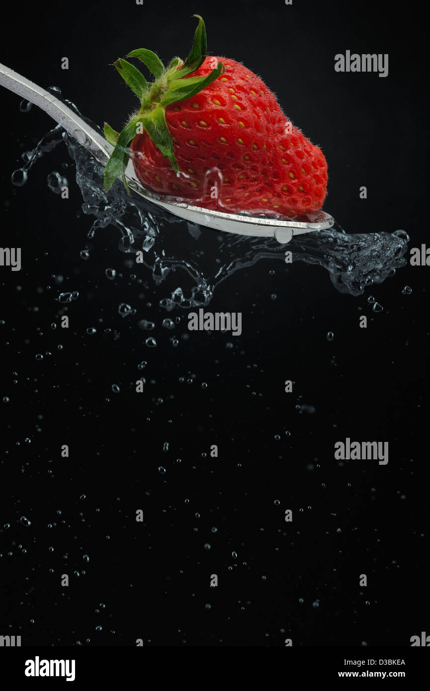 Teaspoon with strawberry and dripping natural mineral water in black ...