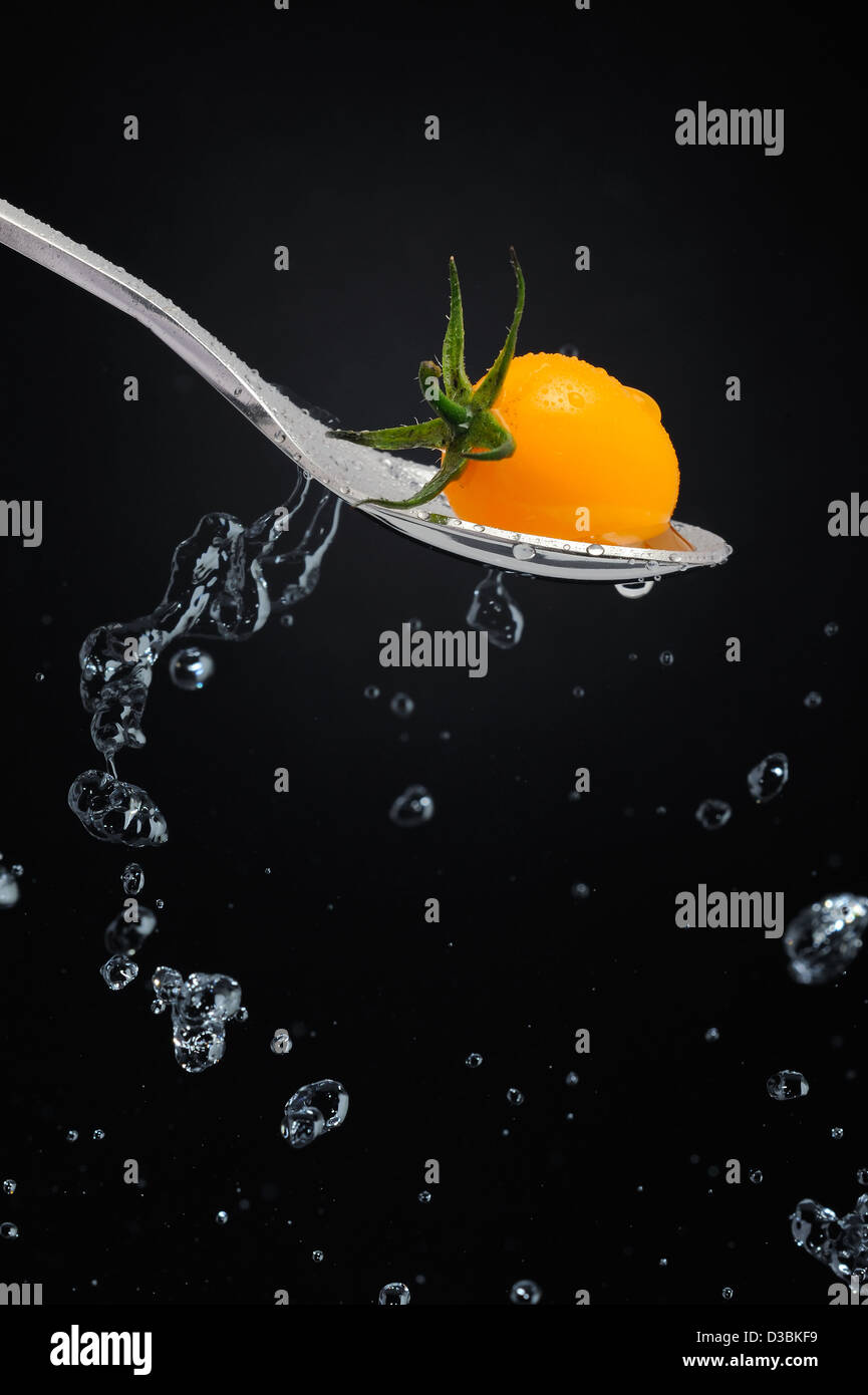 Teaspoon with yellow plum mini tomato and dripping natural mineral ...