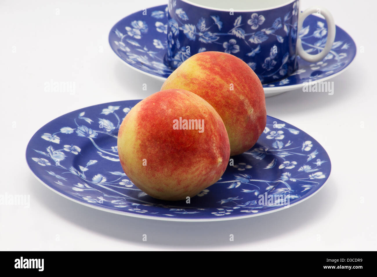 Two peaches on a blue plate on white background Stock Photo - Alamy