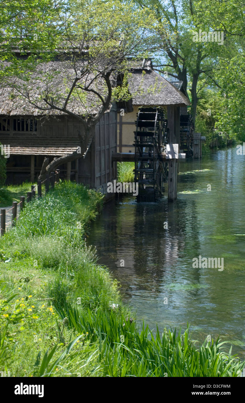 Historic thatched-roof mill houses with river-powered water wheels line ...