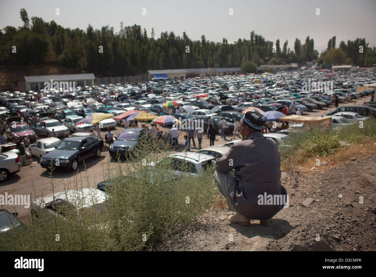 An old man sits on a hill above a 2nd hand car bazaar in Dushanbe ...