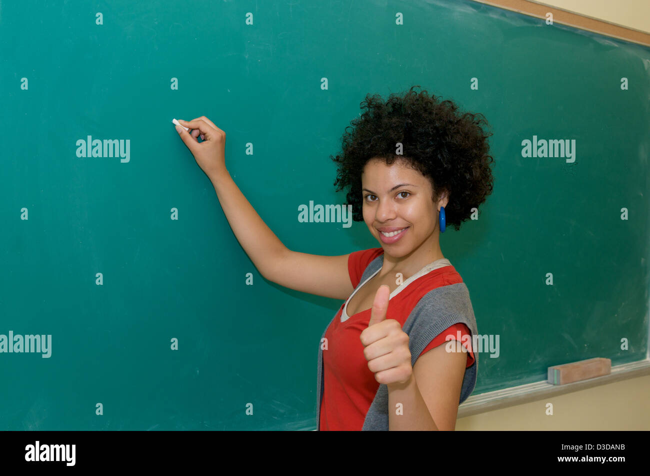 African American student writing on blackboard in classroom with thumbs ...