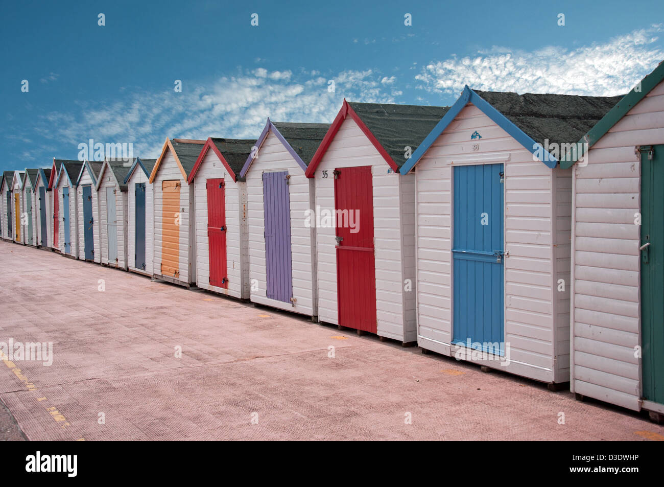 This image shows a row ob beach huts along the promenade with a blue ...