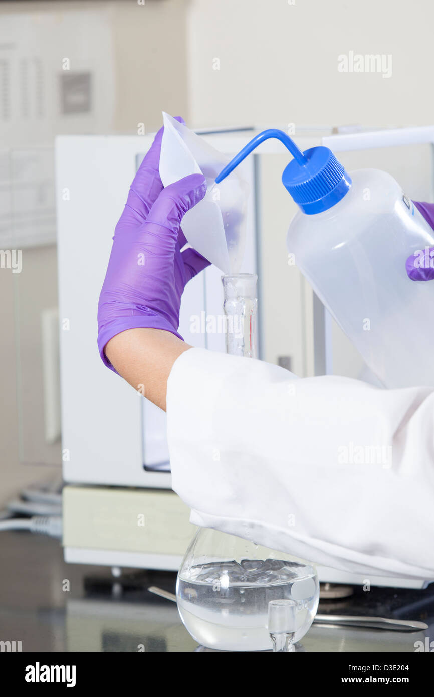 Laboratory scientist washing solid reagent into a water sample in a ...