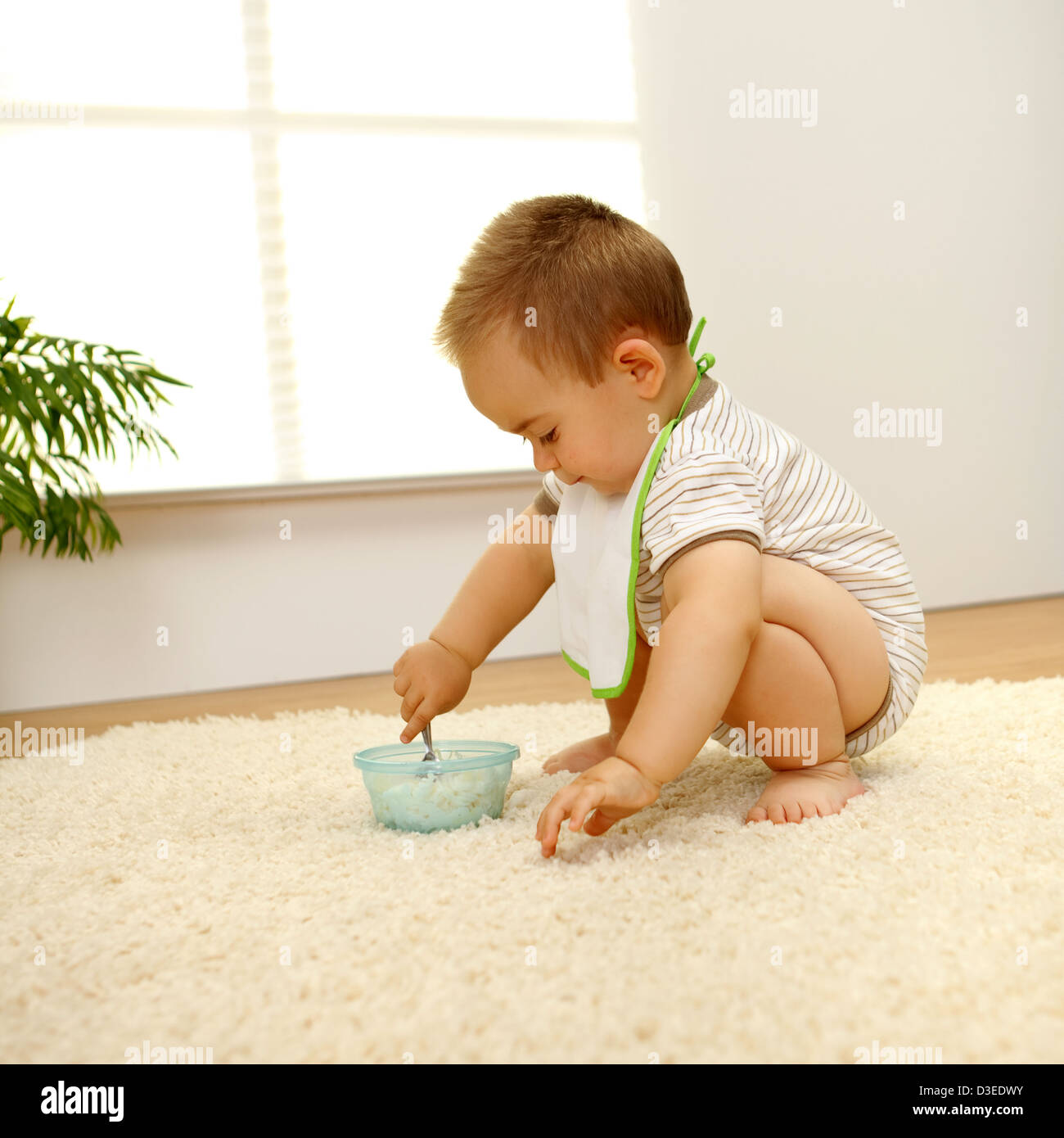 Little baby boy eating alone on white carpet Stock Photo - Alamy