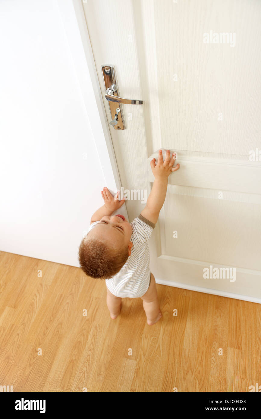 Baby boy crying, wants to reach the door handle. Conceptual view of ...