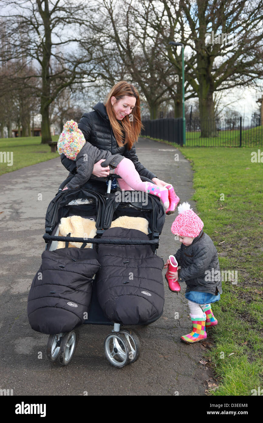 Young mum walking in the park pushing a twin buggy with her twin ...