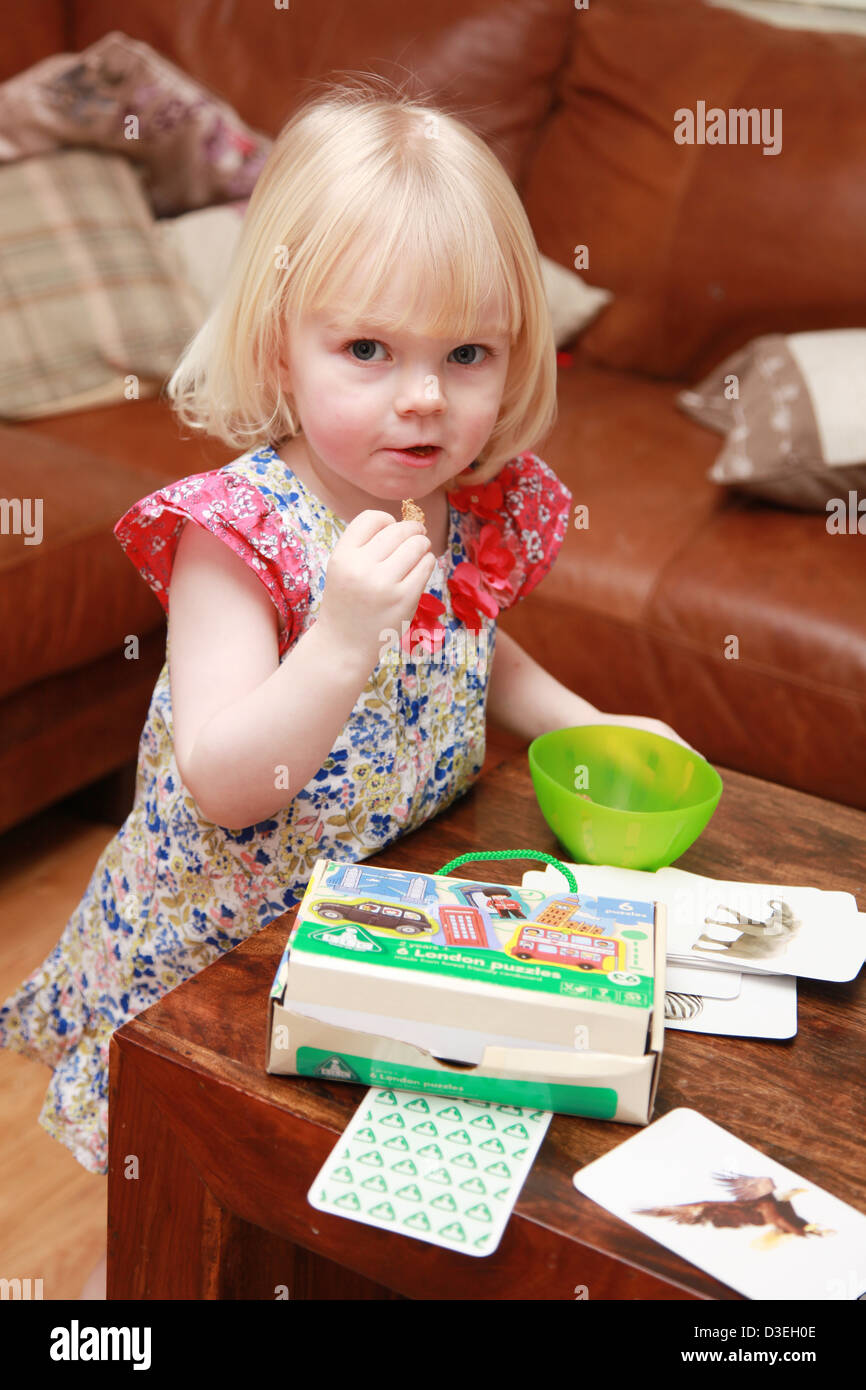 Toddler girl having a drink from a beaker and a snack while playing ...