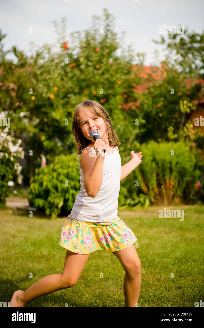 Happy childhood - child singing with microphone outdoor in backyard ...