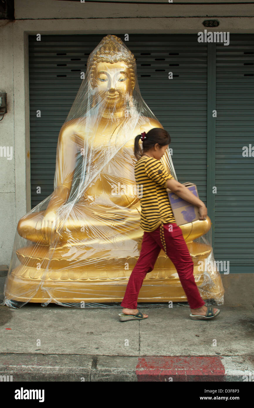 Woman carrying box past wrapped statue of Buddha Stock Photo - Alamy