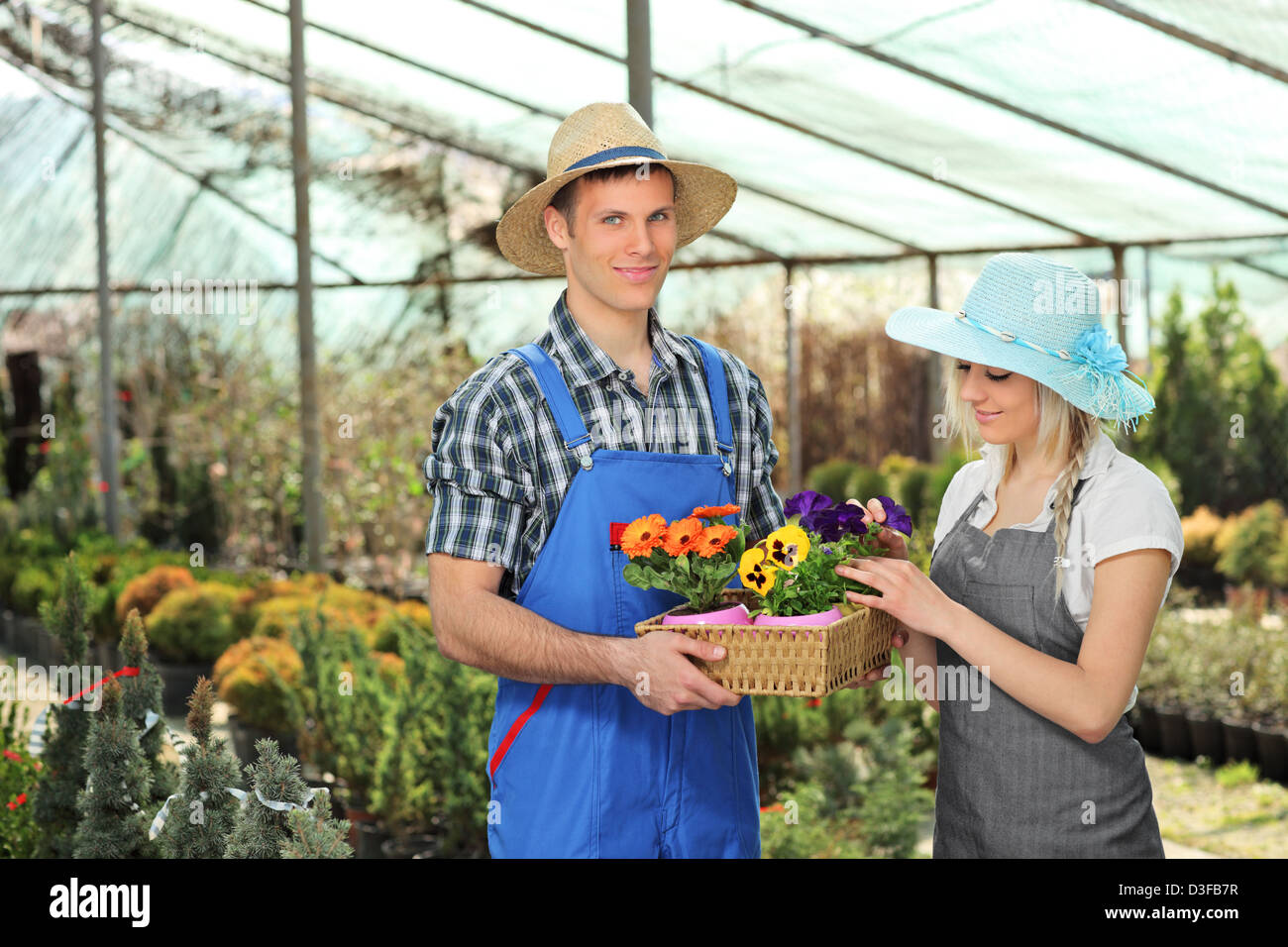 Female and male gardeners with a basket full of flower pots posing in a ...