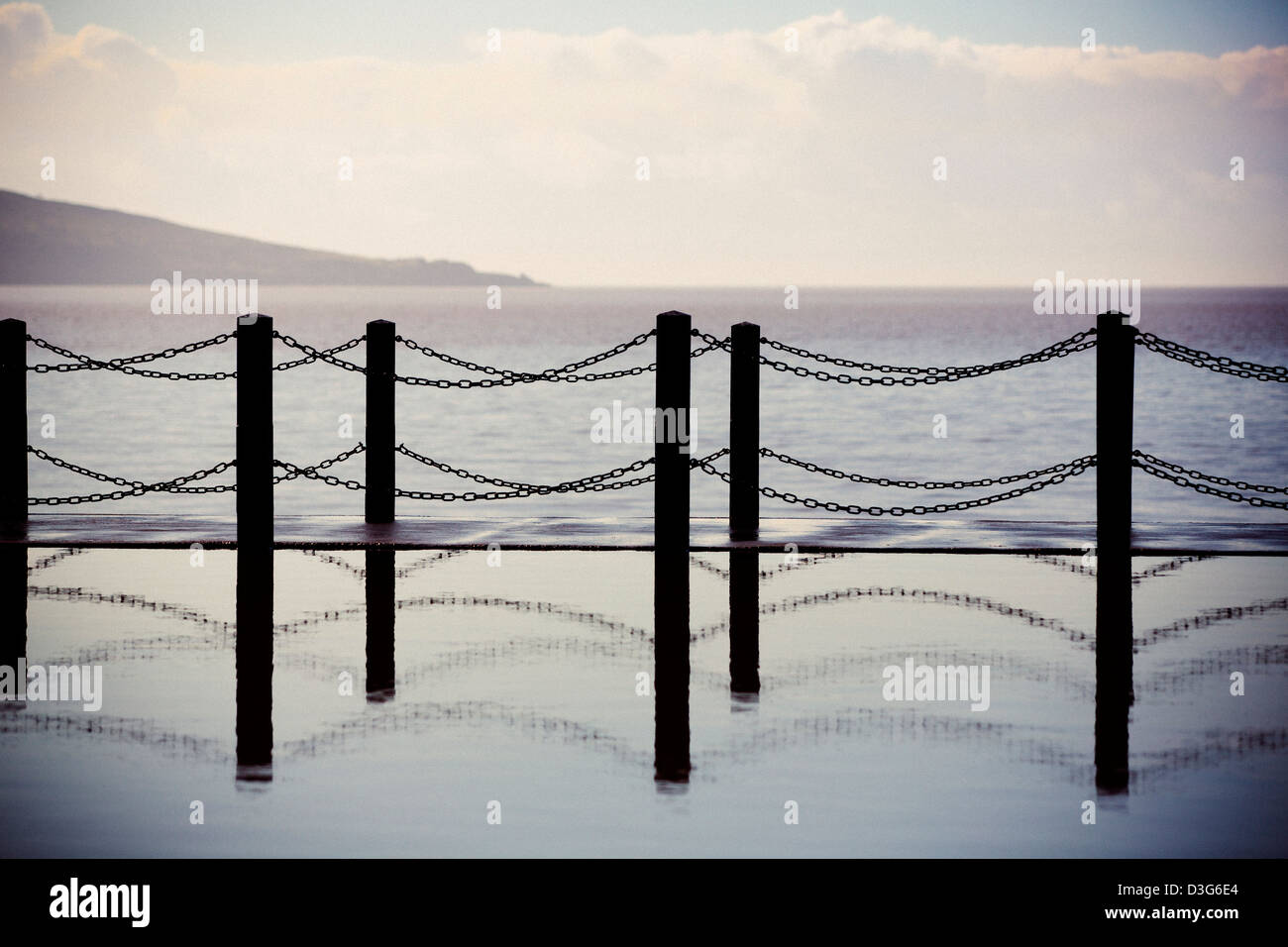 Fence reflected in a pool of water with the sea in the background post ...