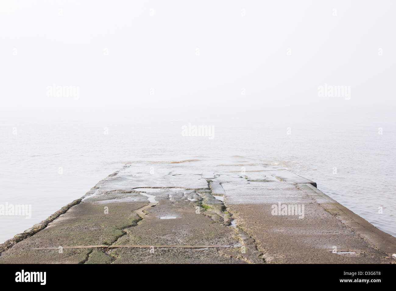 Concrete slipway or walkway descending into the sea shrouded in sea fog ...