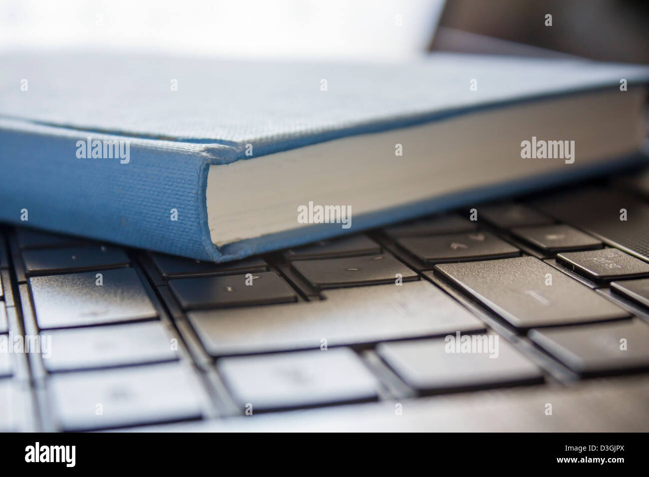 blue book over black computer with window light Stock Photo - Alamy