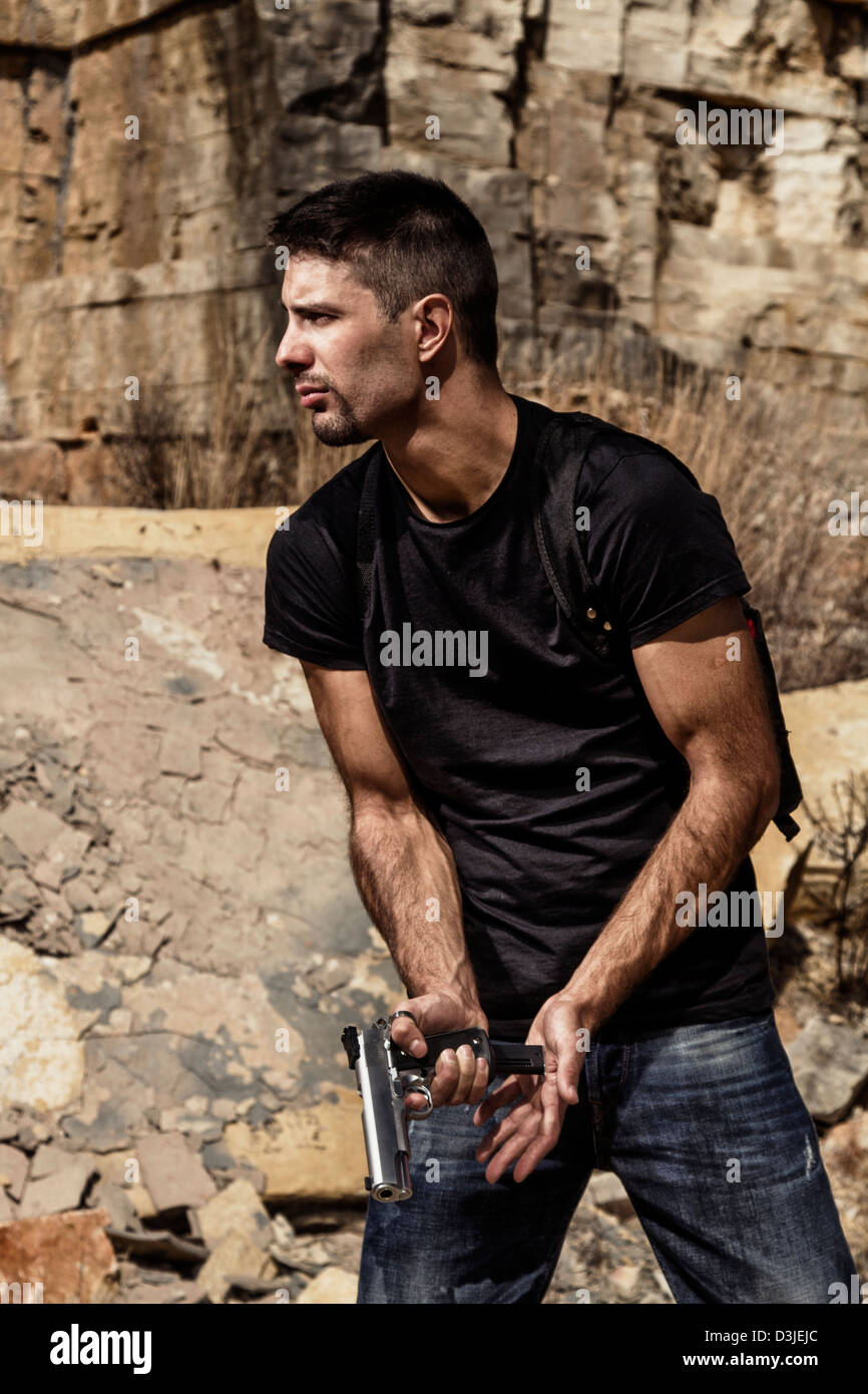 View of a menacing man reloading a handgun in a black shirt and dark ...