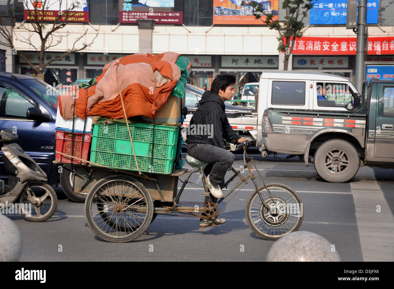Chinese man riding a tricyle heavily loaded in a busy street of ...