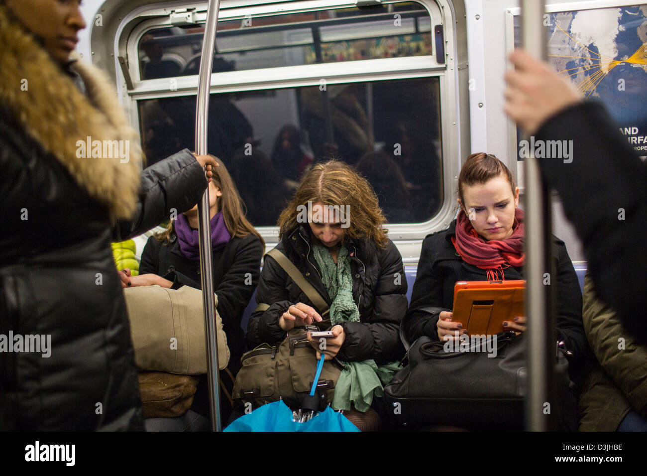 Commuters use their mobile devices while riding the subway in Brooklyn ...