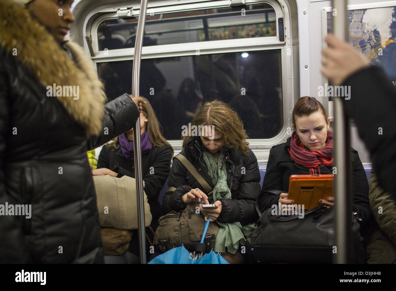 Commuters use their mobile devices while riding the subway in Brooklyn ...