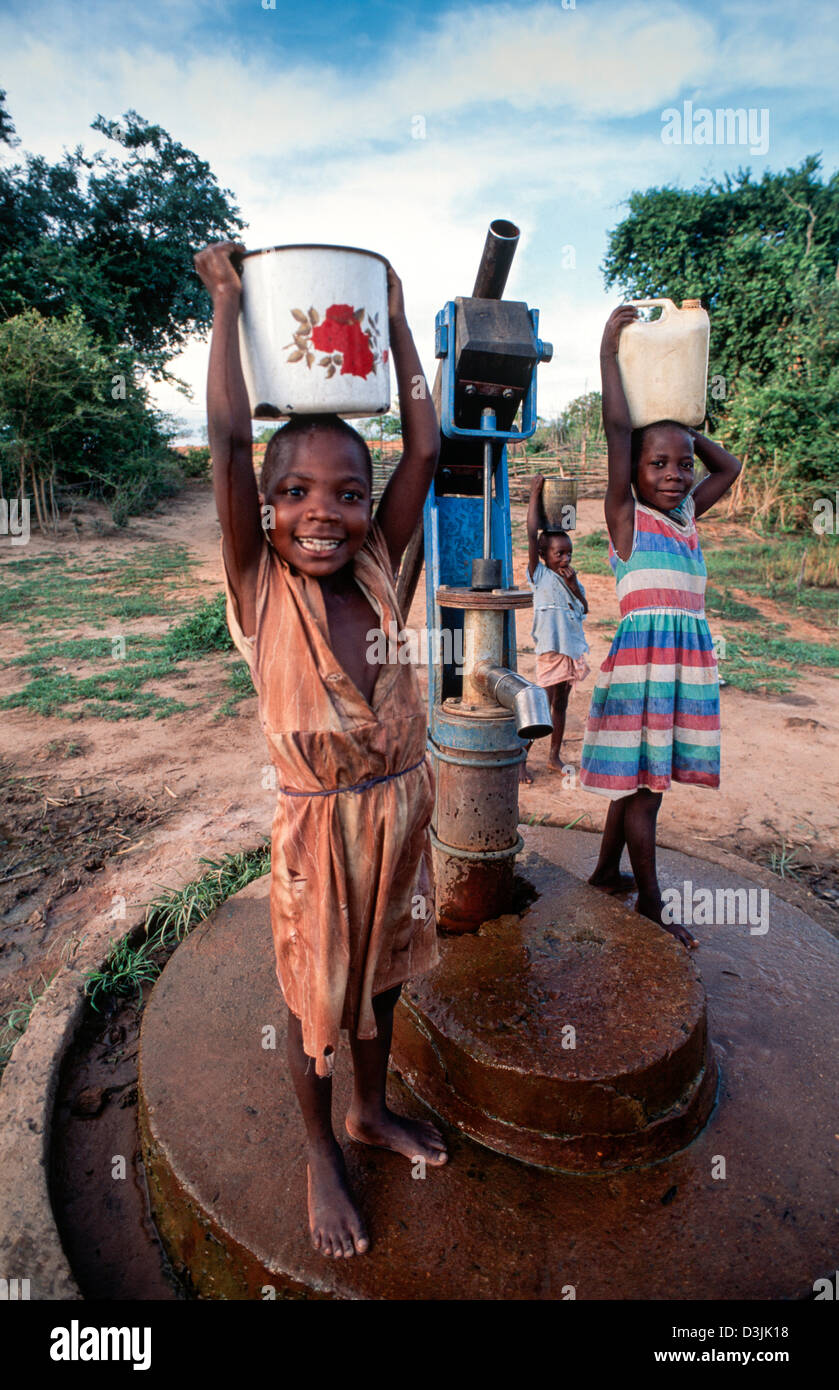 Girls from the Tonga tribe at the village water pump with water cans on ...