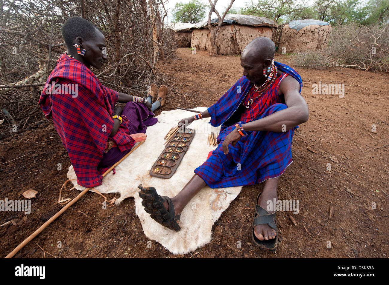 Maasai playing mankala game on a Enkeshui board in the manyatta ...