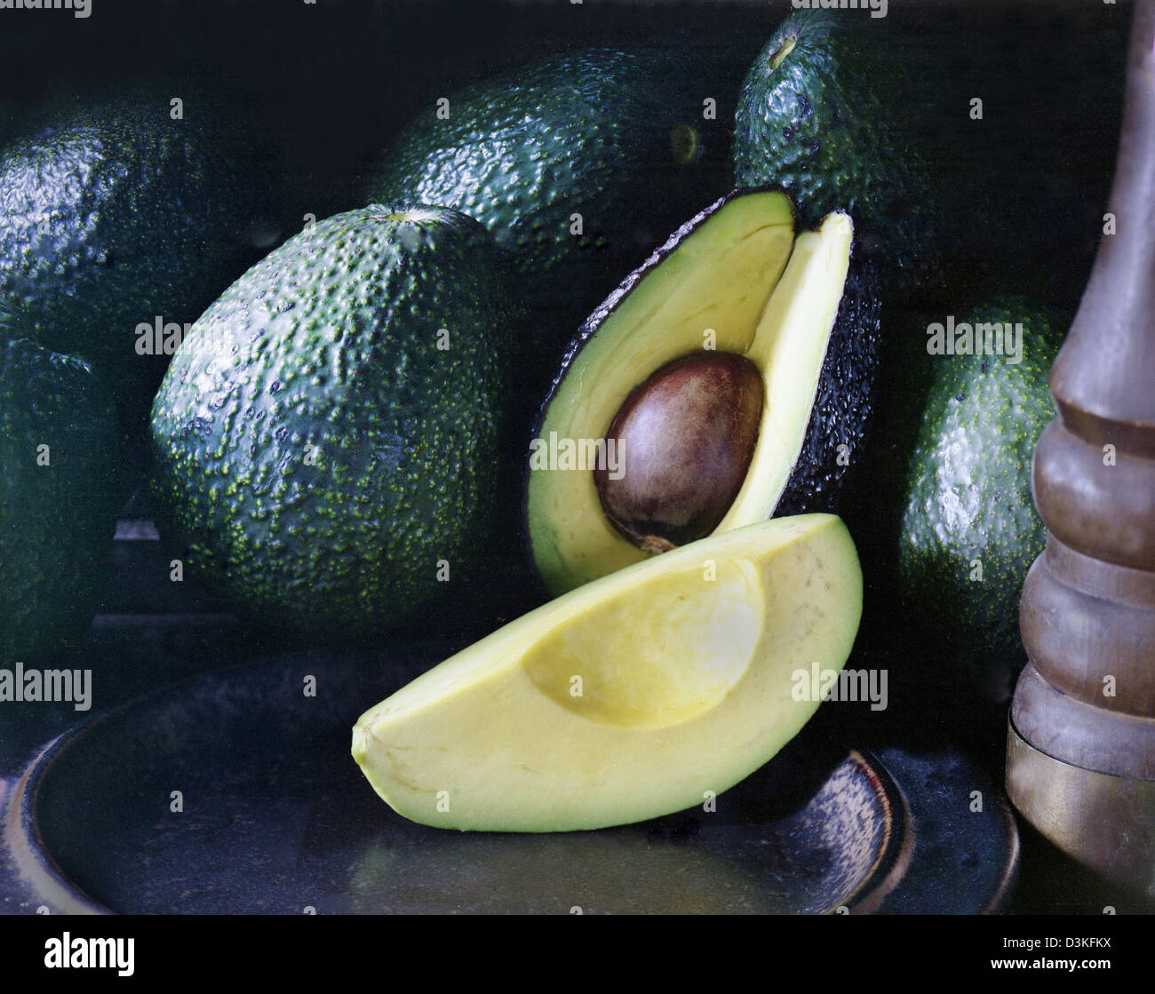 Ripe avocado sliced open on a brown plate, including other avocados in ...