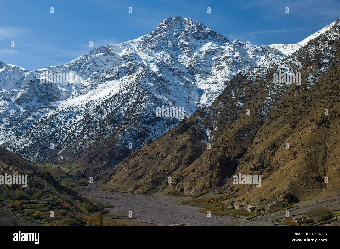 Dwellings along the stony river valley, with snow-capped mountains ...