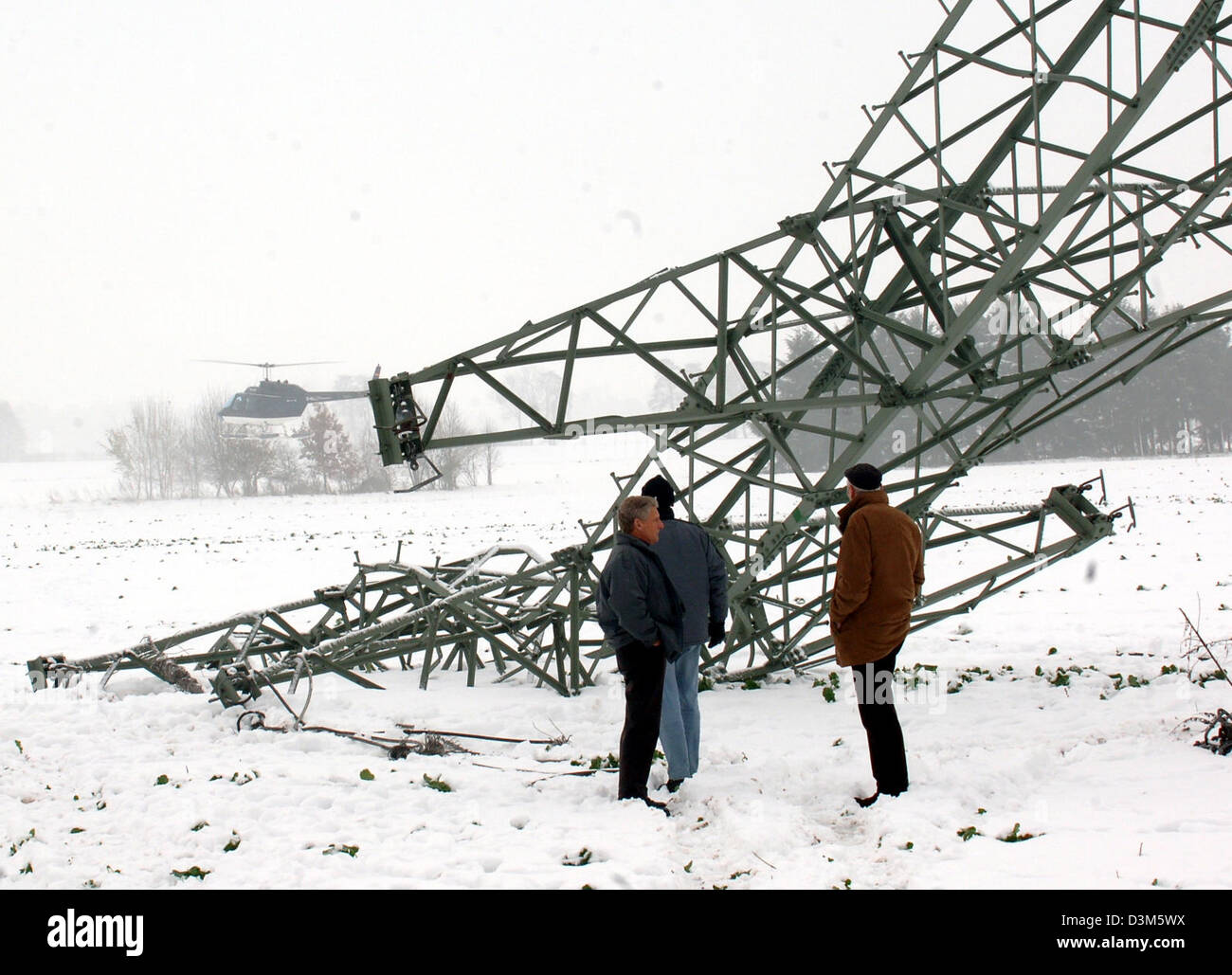 (dpa) - Men stand next to a broken high tension pylon on a field near ...