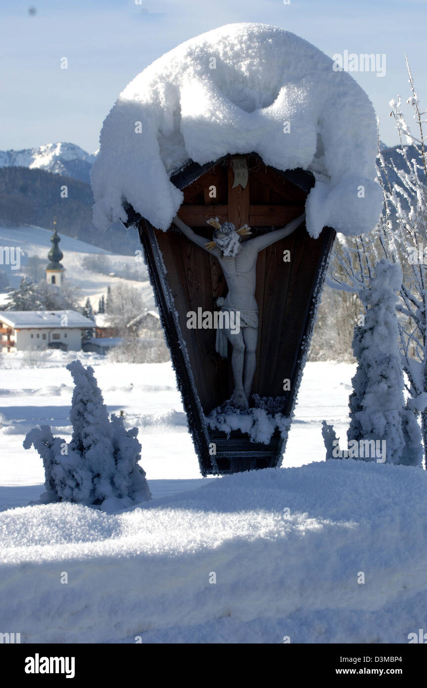 The picture shows a snow covered wayside cross with the spire of St ...