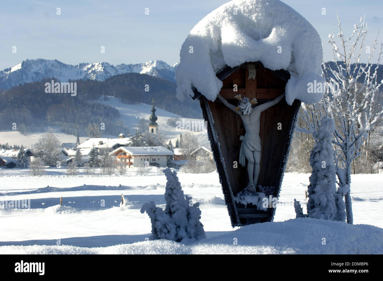 The picture shows a snow covered wayside cross with the spire of St ...