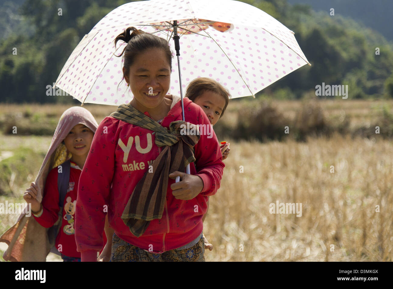 A woman and her two children walk along the rice paddy walls on their ...