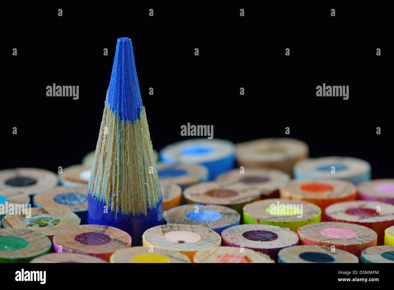 A sharp blue crayon against black background with out of focus crayon ...