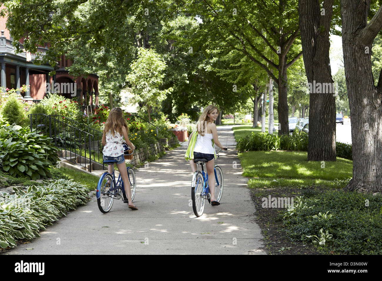 Teen sisters riding bikes on sidewalk Stock Photo - Alamy