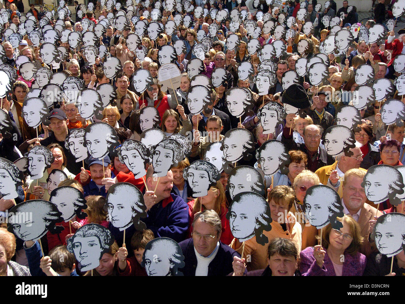 A crowd of people present masks which depict Wolfgang Amadeus Mozart ...