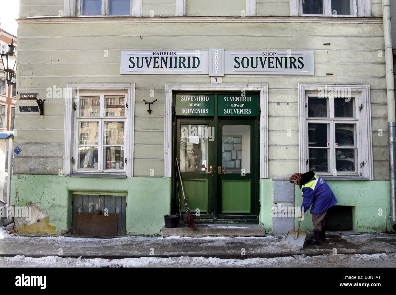 Awoman shovels snow off a souvenir shop in the Old Town of Tallinn ...