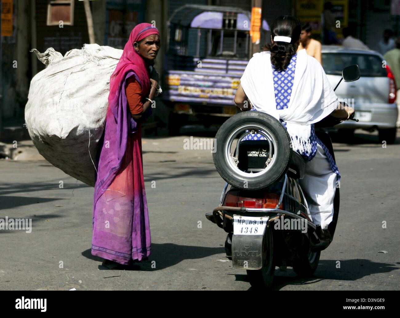 An elderly Indian woman, carrying a heavy sack, waits until a young ...