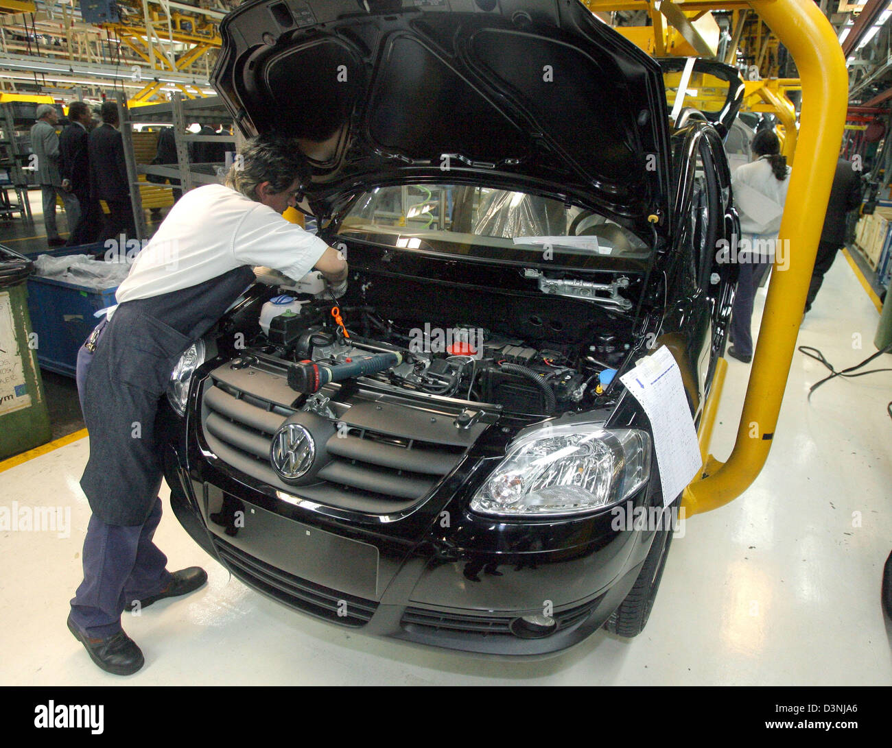 An employee works on a car's engine compartment in the Volkswagen ...