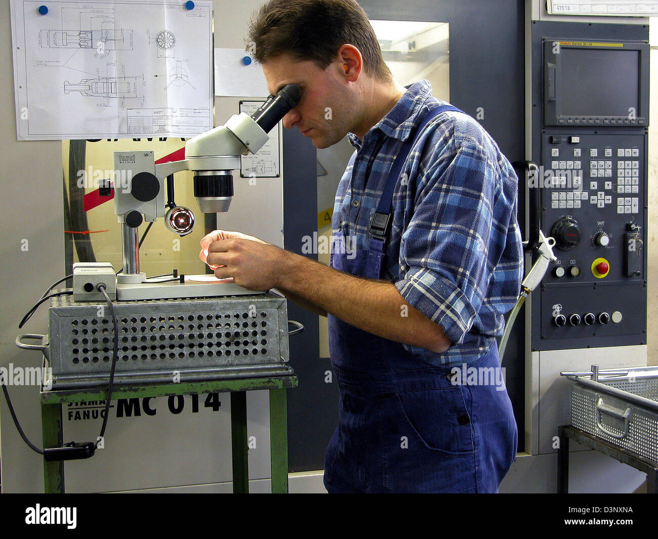 An employee of Roth Company observes a workpiece through a microscope ...