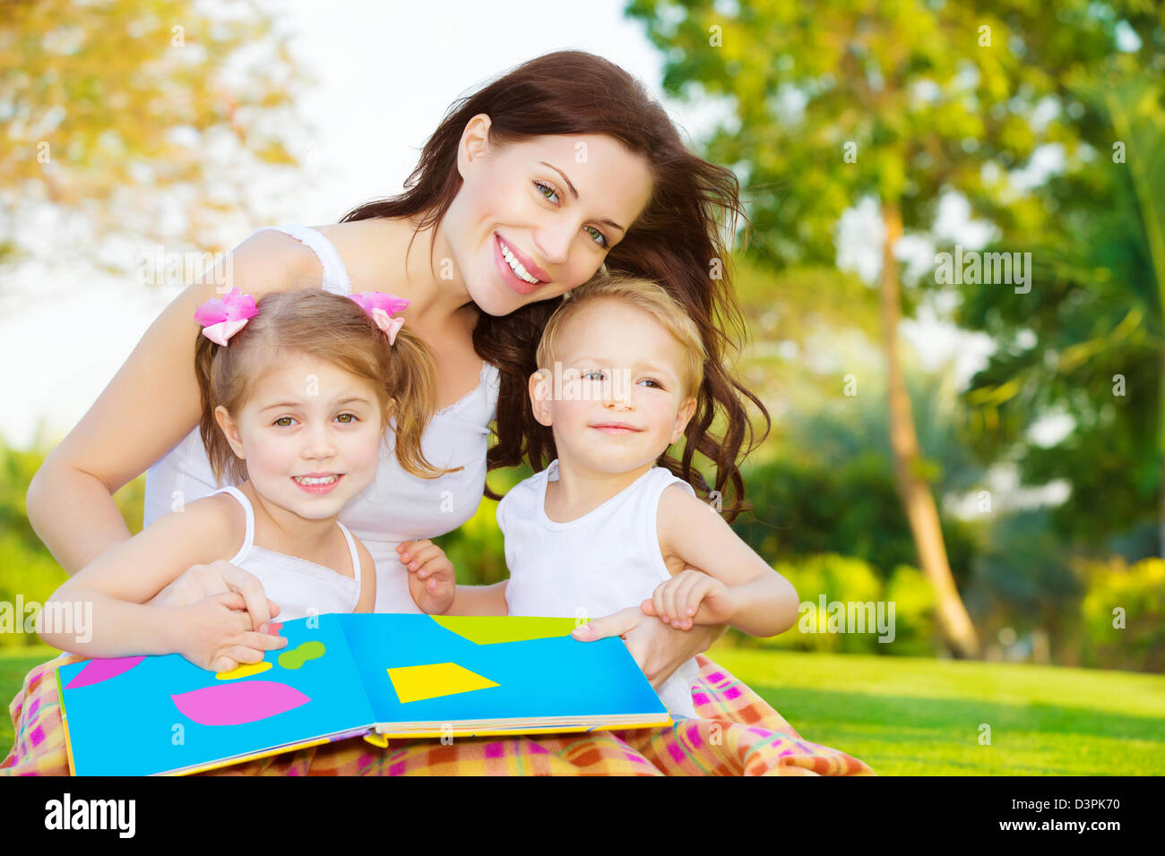 Image of cute young female with two little children read book outdoors ...