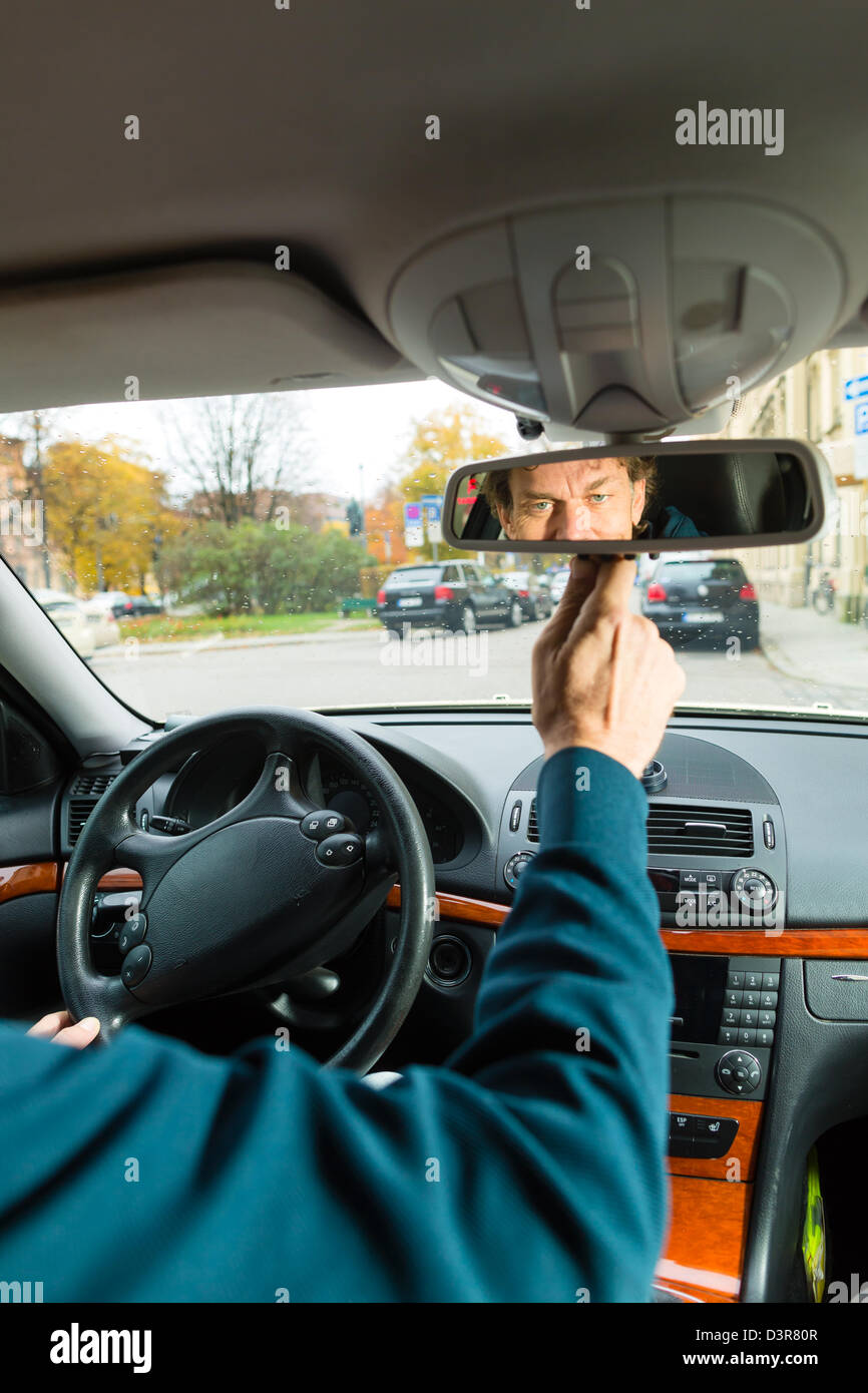 Experienced taxi driver is looking in the rear view mirror in his taxi ...
