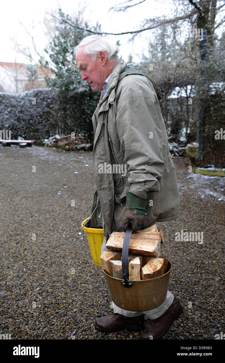 Pensioner carrying logs from log shed at home in north yorkshire uk ...