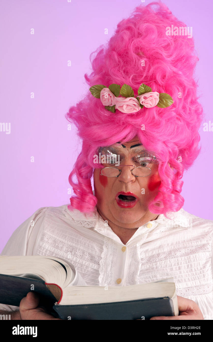 Pink wig pantomime dame expressing shock reading large saucy book Stock ...