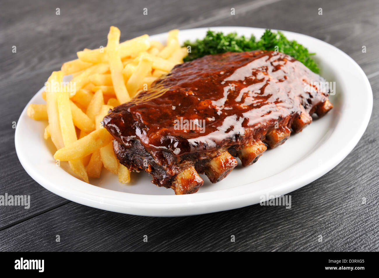 Grilled juicy barbecue pork ribs in a white plate with fries and ...