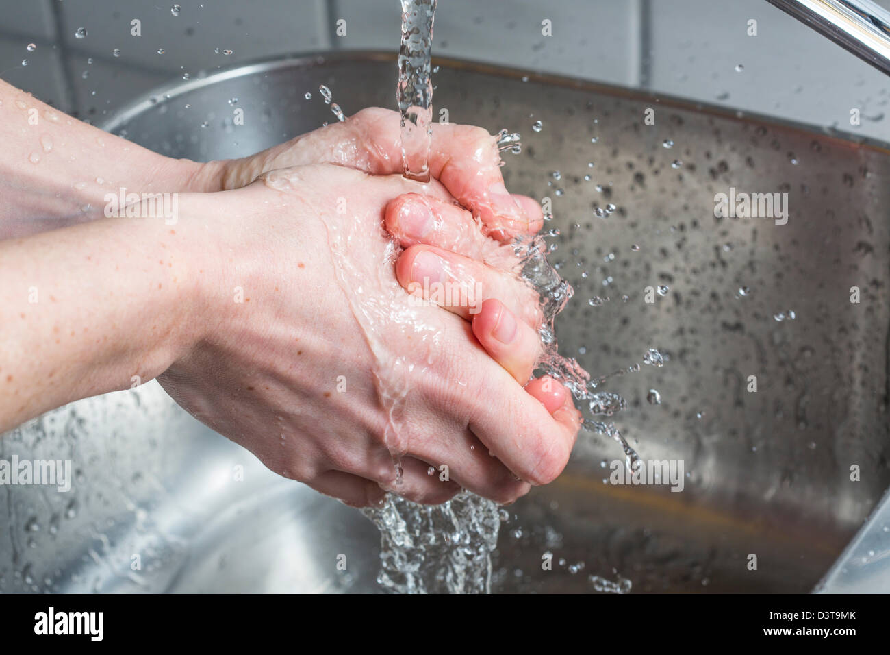 Person is washing her hands under running water from a tap in a bathroom. Symbol image for water ...
