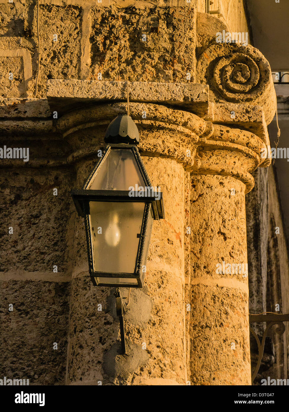 A black wrought iron traditional street lamp hangs from a pitted stone ...