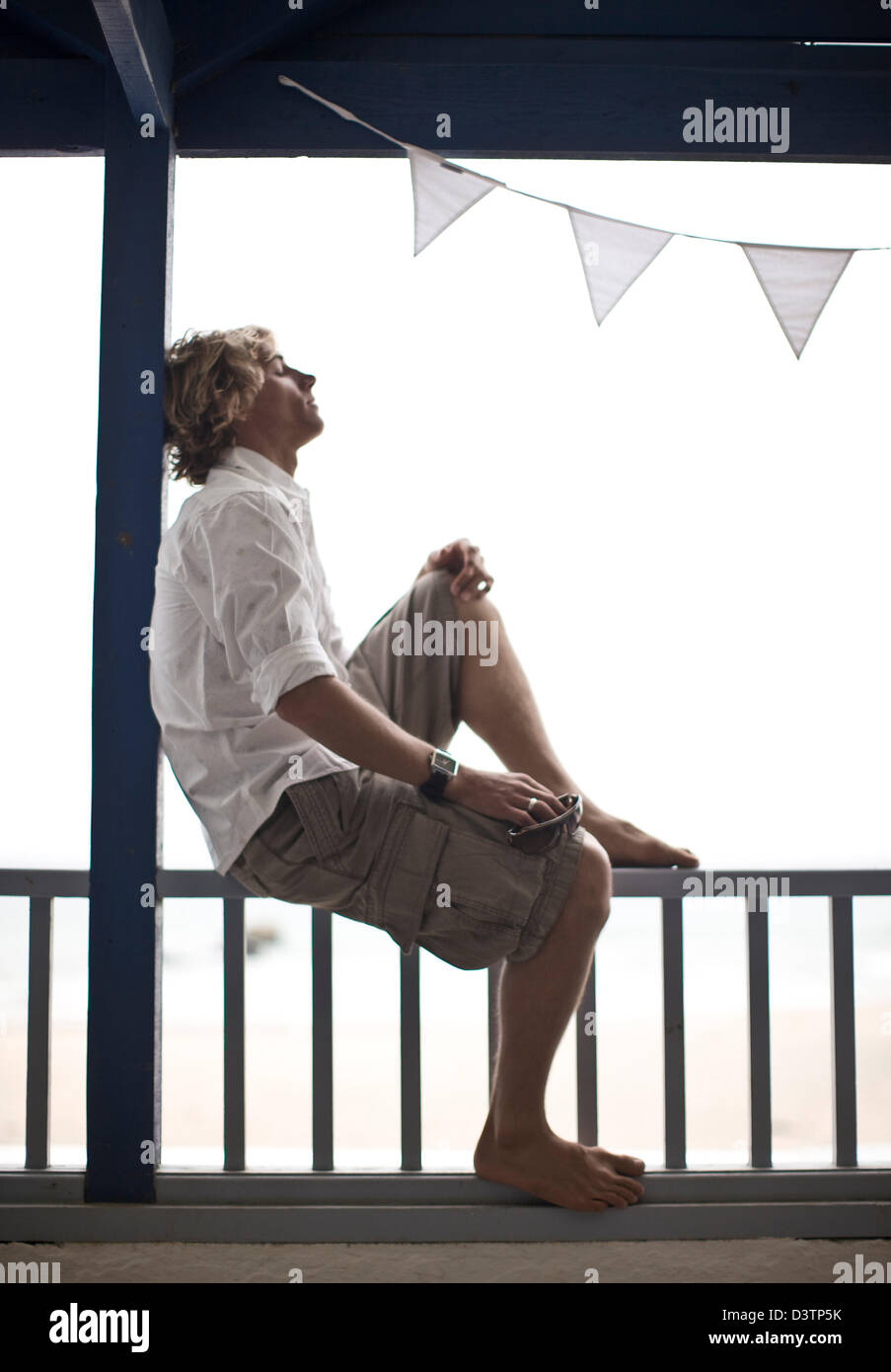 Young man sits on balcony railings with eyes closed, St Agnes, Cornwall ...