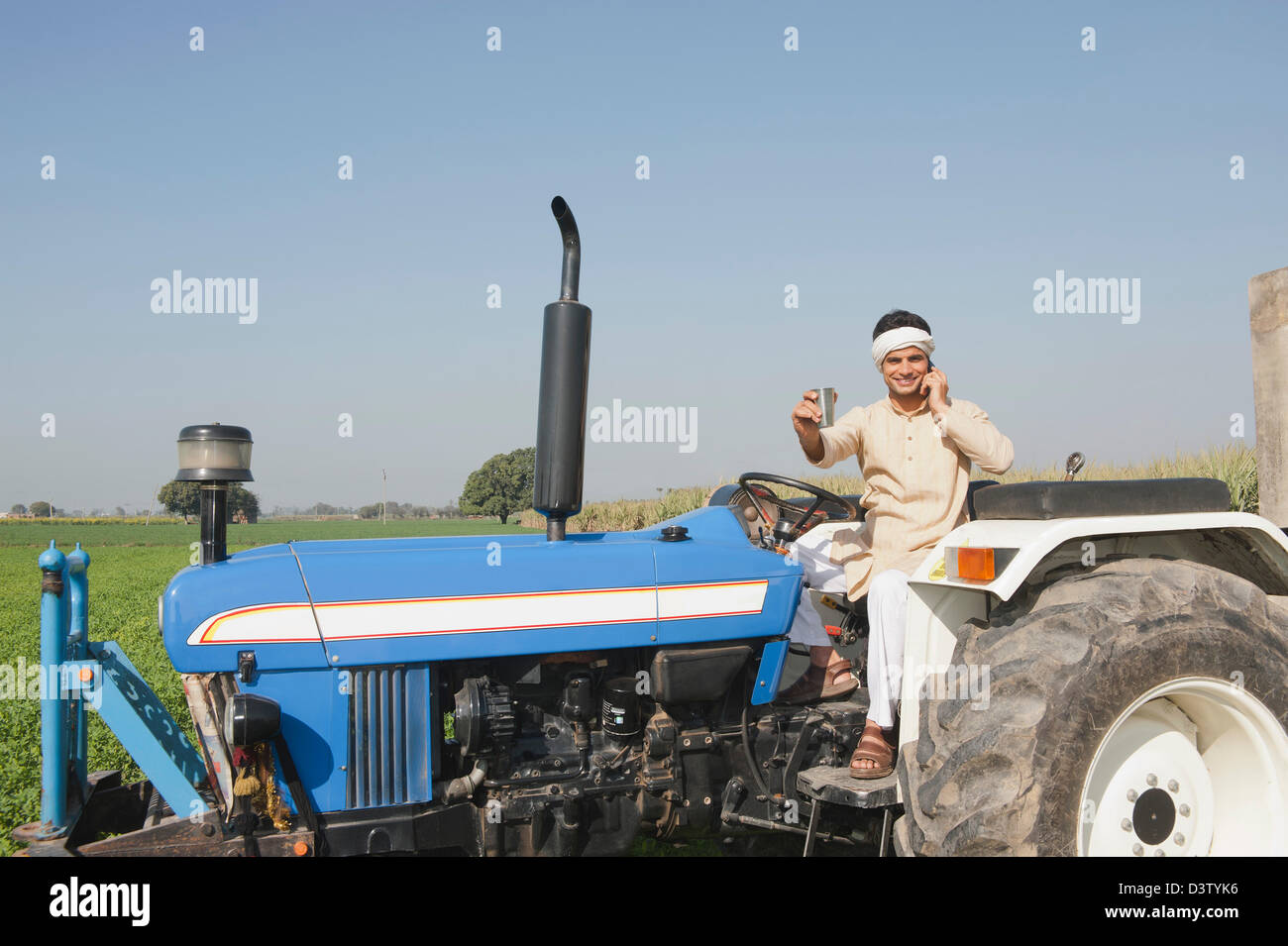 Farmer driving a tractor and talking on a mobile phone in the field ...