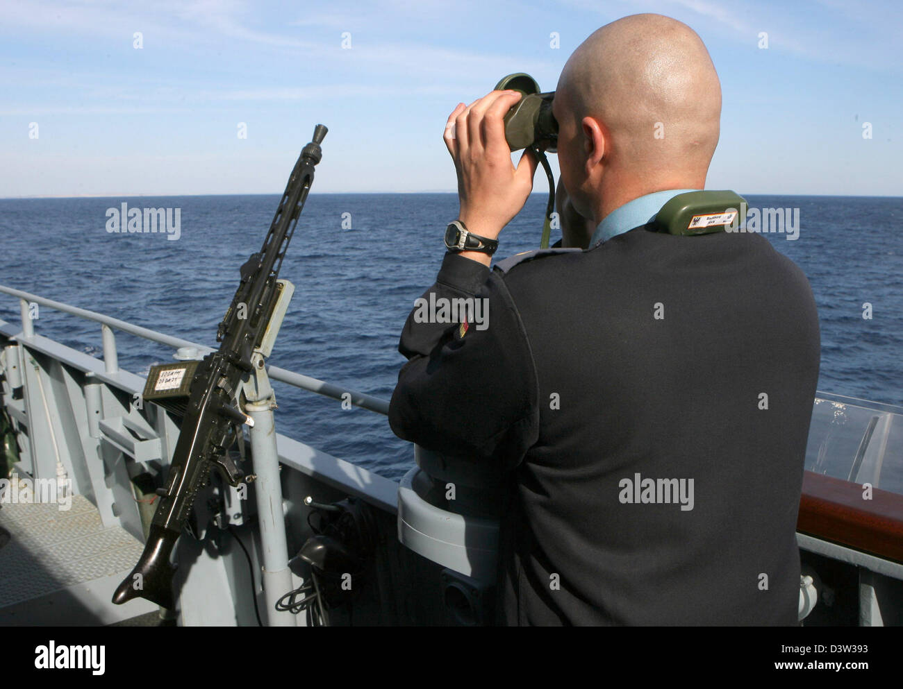 A seaman of the German Navy watches the sea through binoculars next to ...