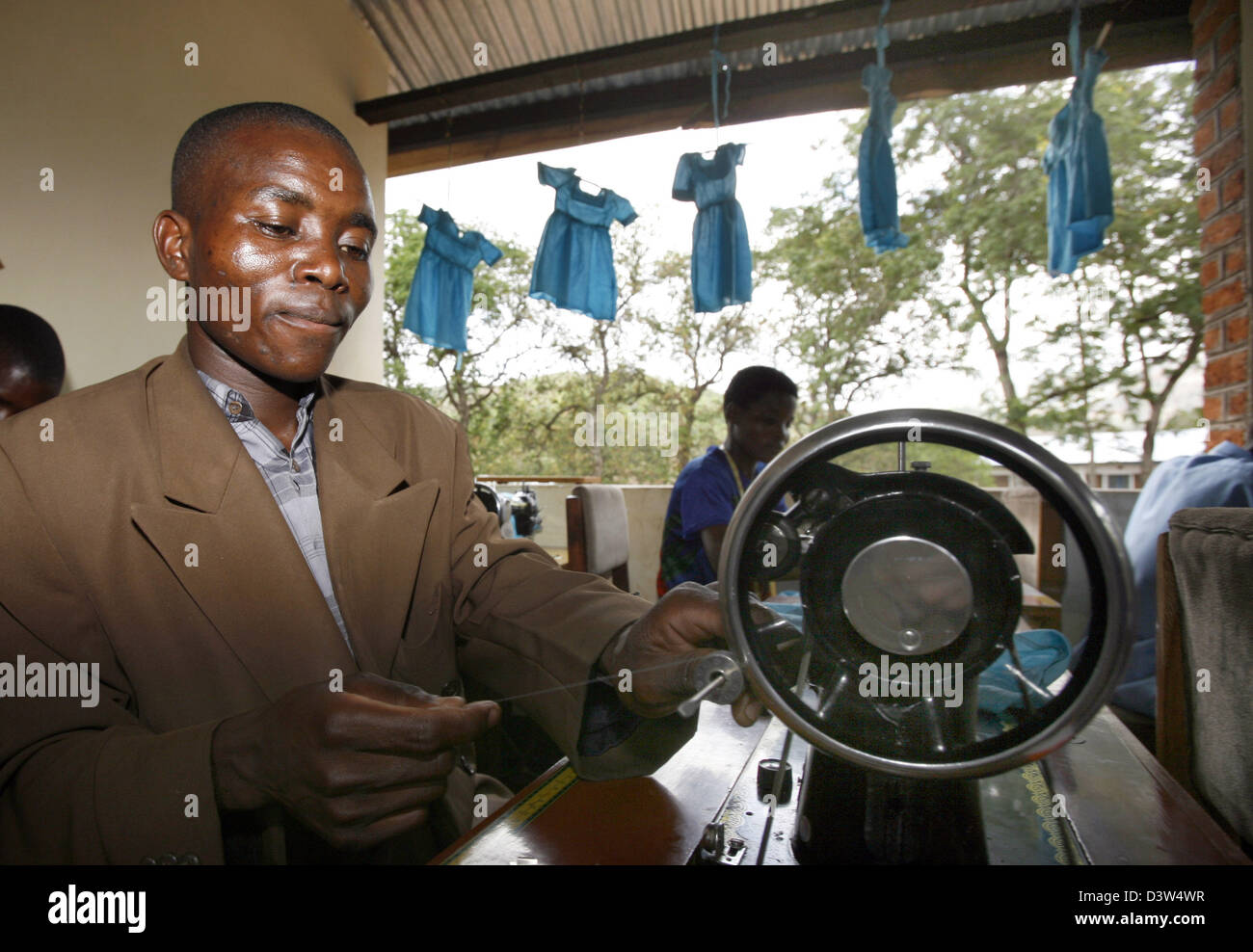 A man sews blue shirts on a sewing machine at a tailor's workroom in ...