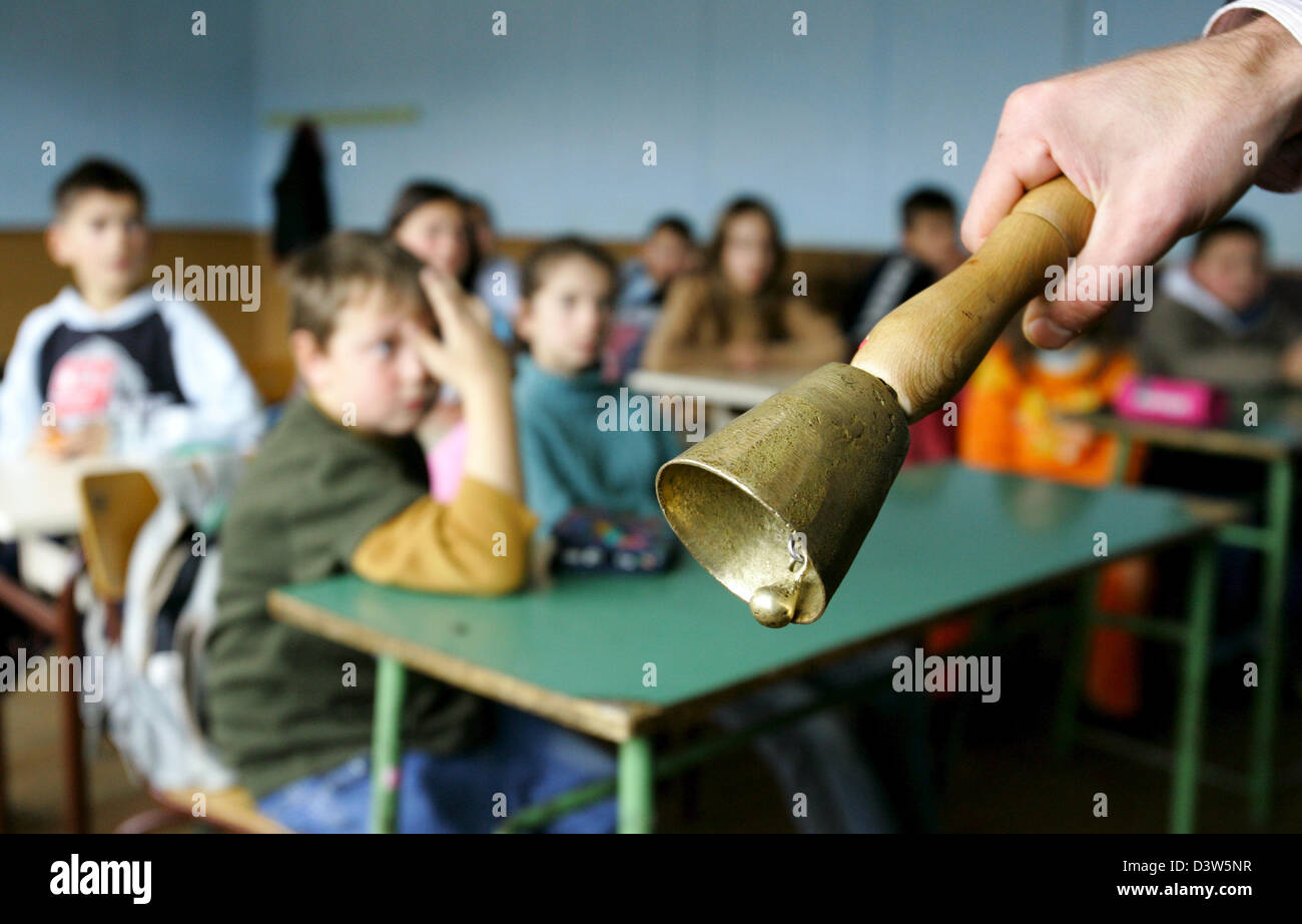The picture shows a teacher's hand ringing the school bell in a ...